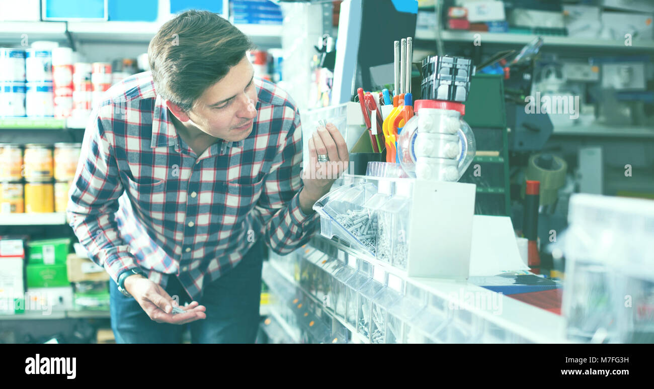 smiling man standing near the counter and buying fasteners, screws ...