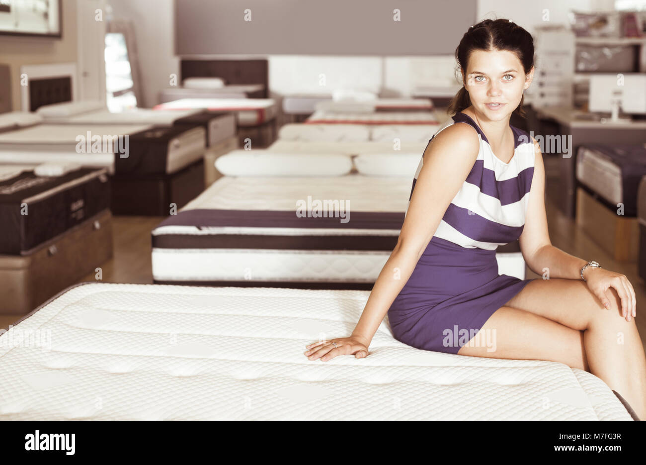 positive brunette female is sitting on mattress for testing it in the ...