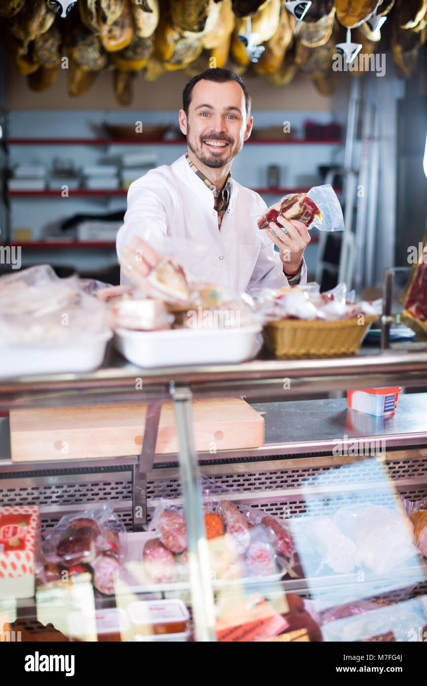 Smiling man seller showing sorts of meat in butcher’s shop Stock Photo ...