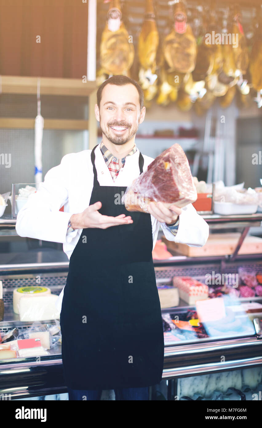 Happy adult seller offering piece of meat in butcher’s shop Stock Photo ...