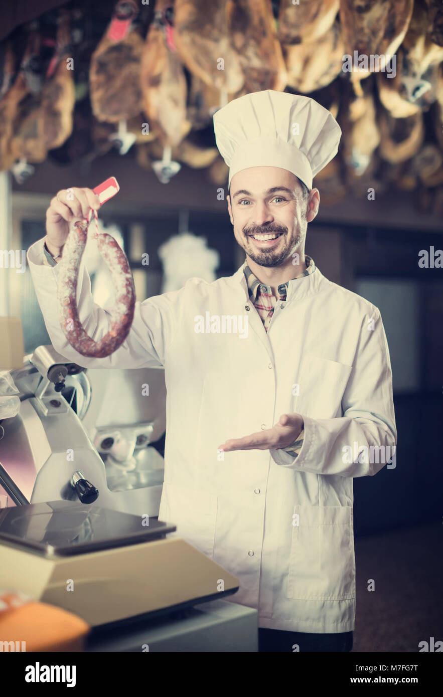Happy European Male Shop Assistant Using Scales For Sausage In Butcher
