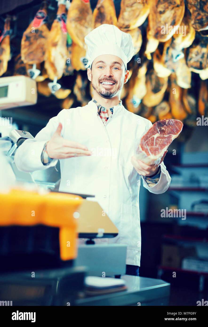 Smiling man butcher showing piece of meat in butcher’s store Stock ...
