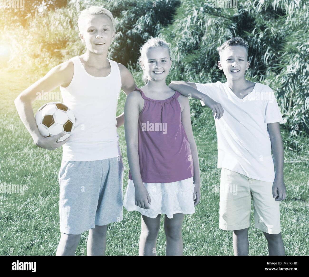 Portrait of happy positive children standing with ball in green summer ...