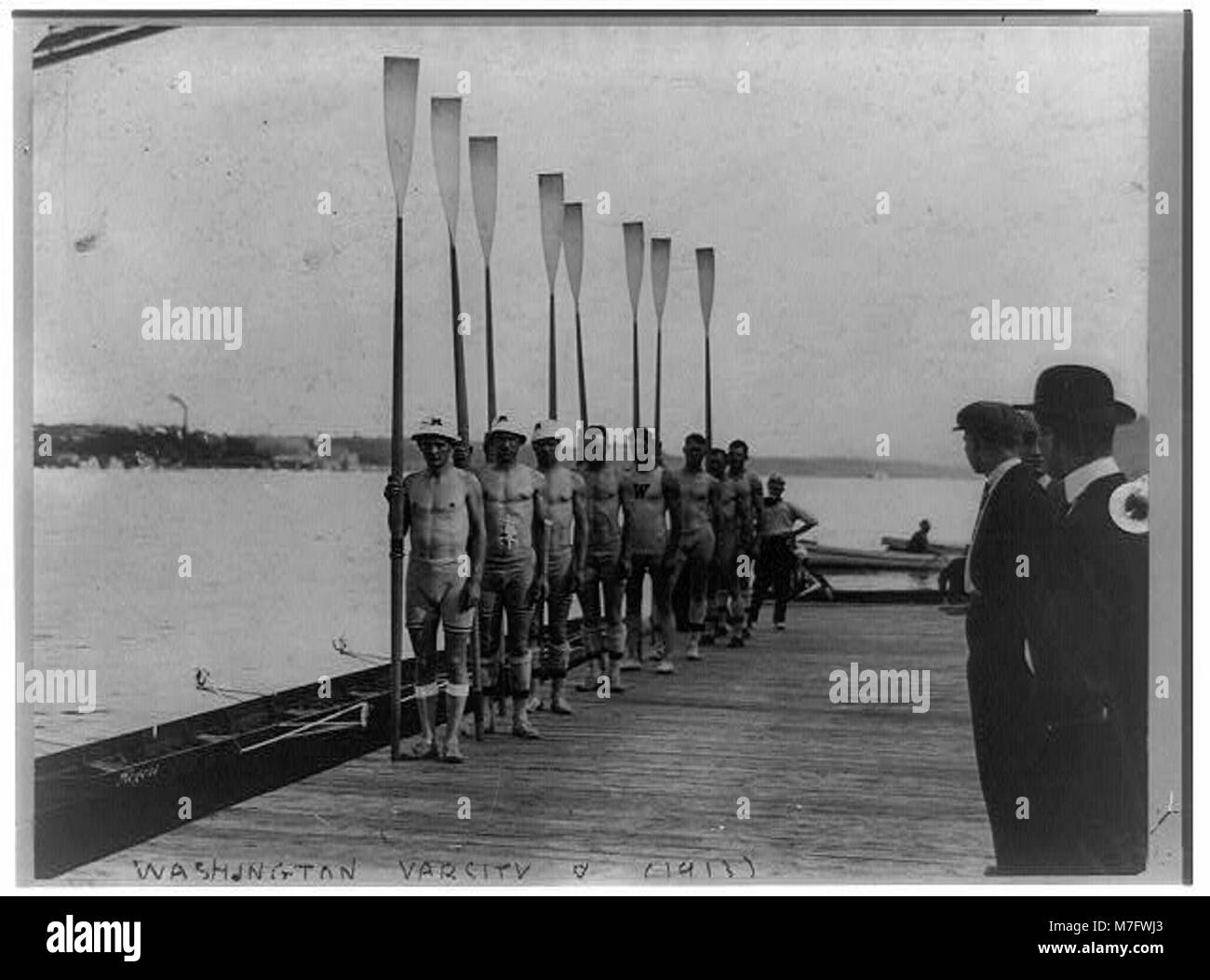 Washington Varsity 8 rowing team posed on dock holding oars ...