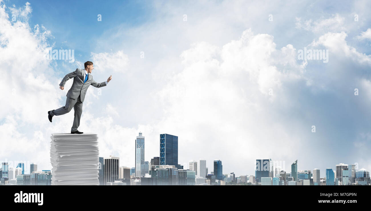 Businessman in suit running with phone in hand on pile of documents ...