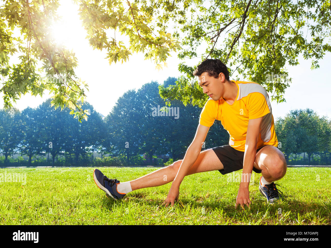 Young sportsman stretching legs before workout at city park in summer ...