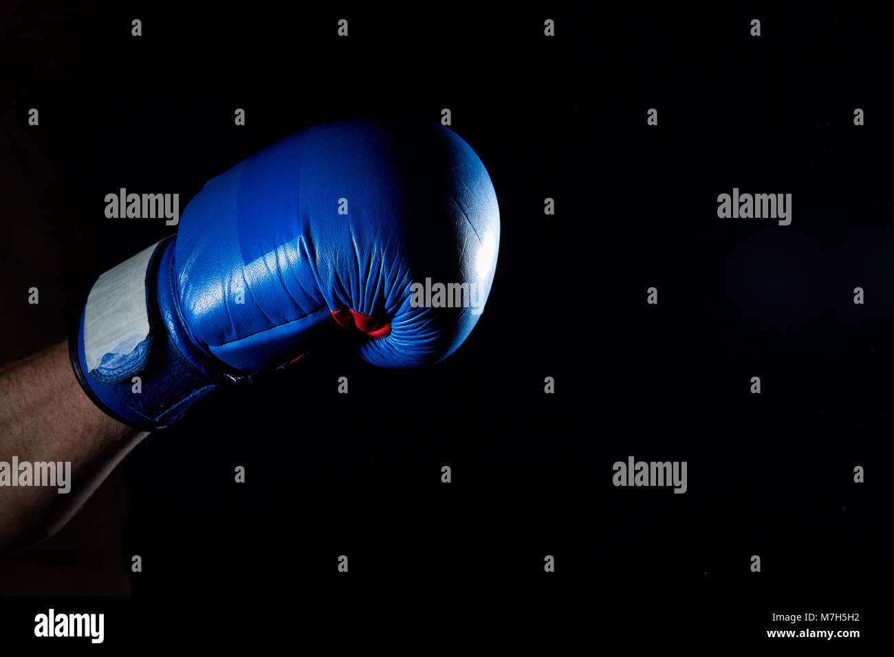 A fighter's blue boxing gloves on his hand isolated over dark blurred ...