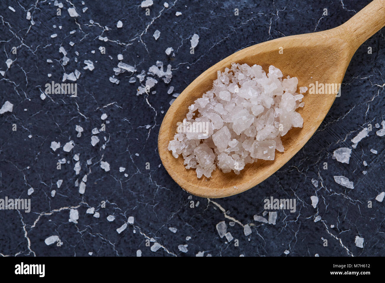 Sea salt crystals in a wooden spoon on dark marble backgrond, top view ...