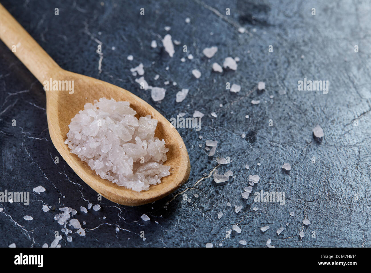 Sea salt crystals in a wooden spoon on dark marble backgrond, top view ...