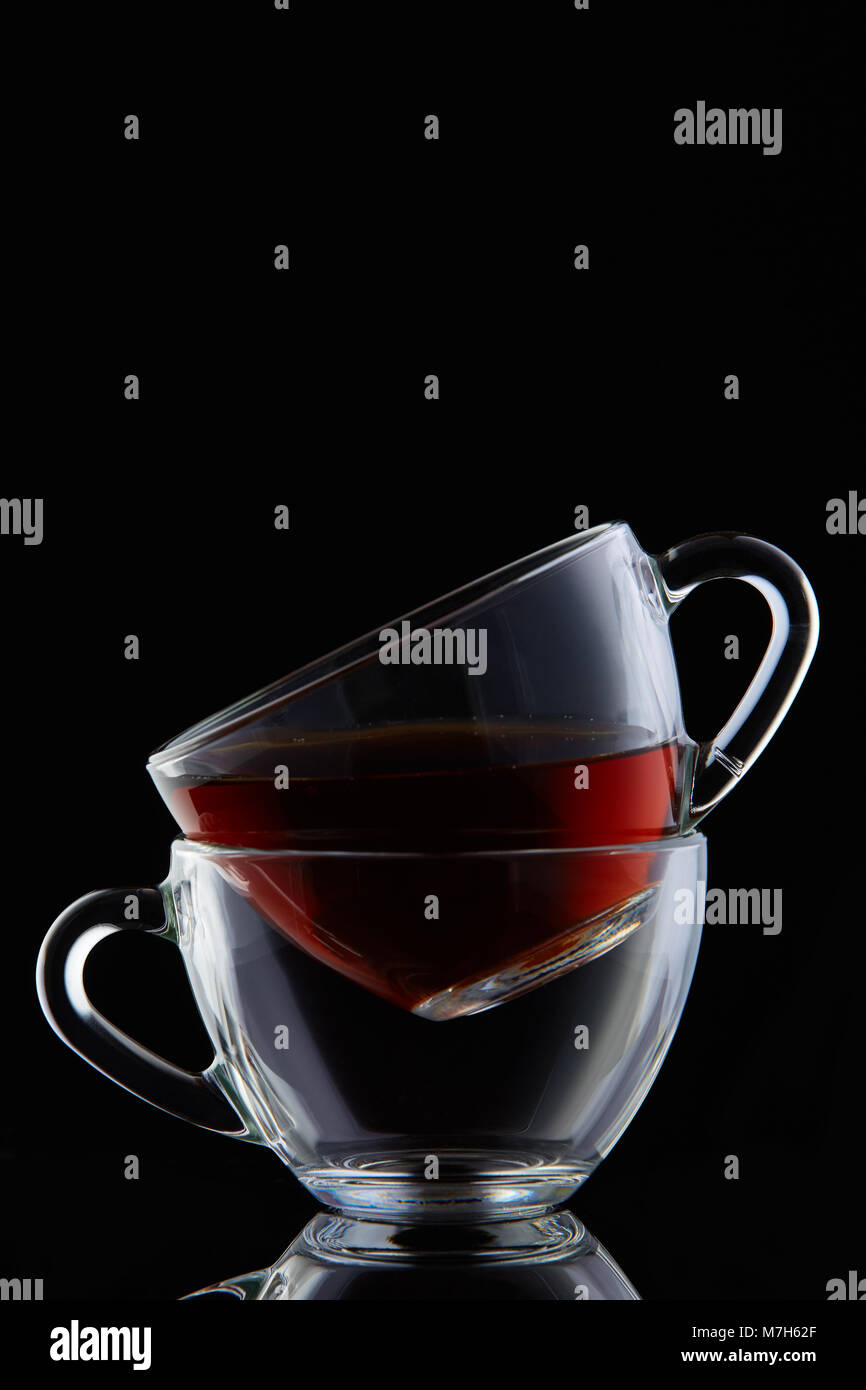 Conceptual composition of two glass teacups over colored red background ...