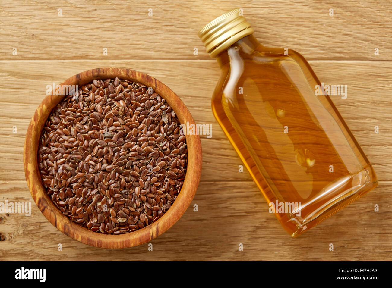 Flax seeds in clay ceramic bowl and flaxseed oil in transparent glass bottle on wooden ...