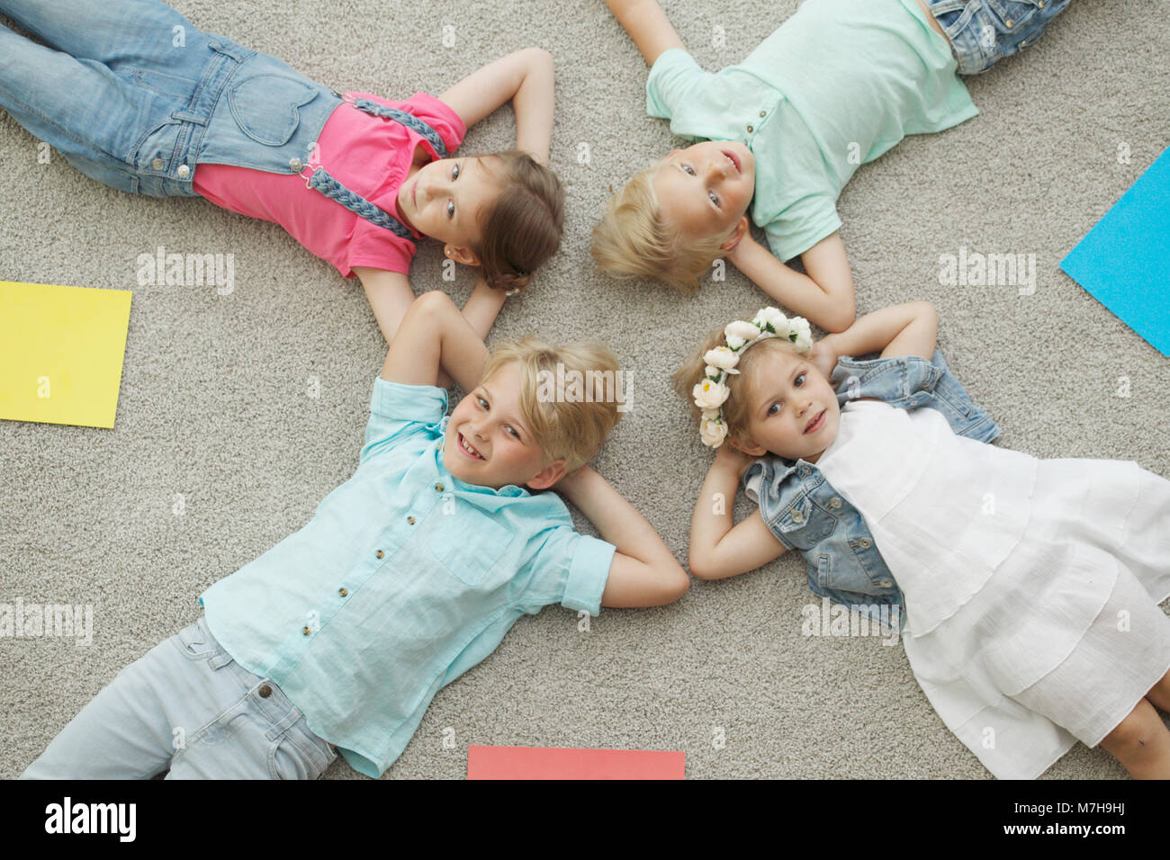 Four happy children laying on floor and smiling among colorful paper ...