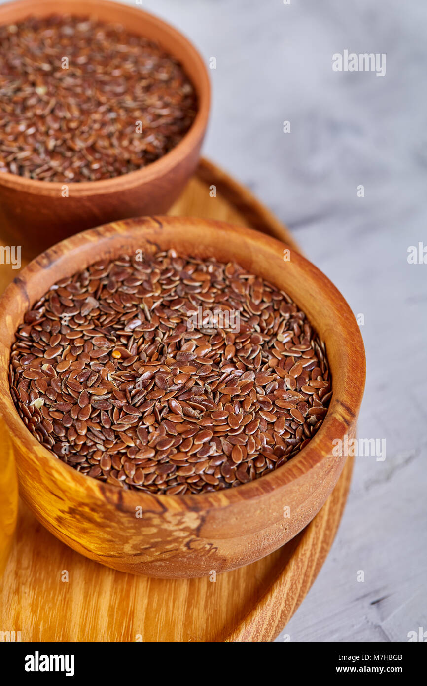 Flax seeds in clay ceramic bowl and flaxseed oil in transparent glass bottle on light textured ...