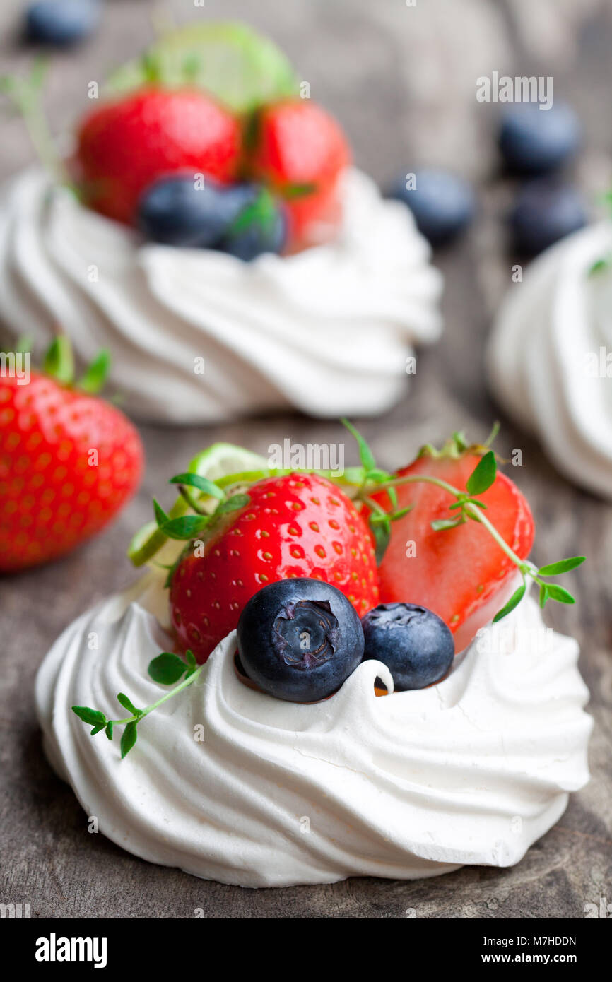 Mini Pavlova meringue cakes with berries and lime on rustic wooden ...