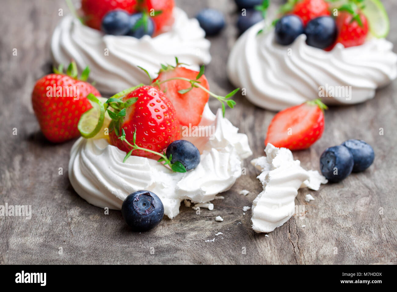 Mini Pavlova meringue cakes with berries and lime on rustic wooden ...