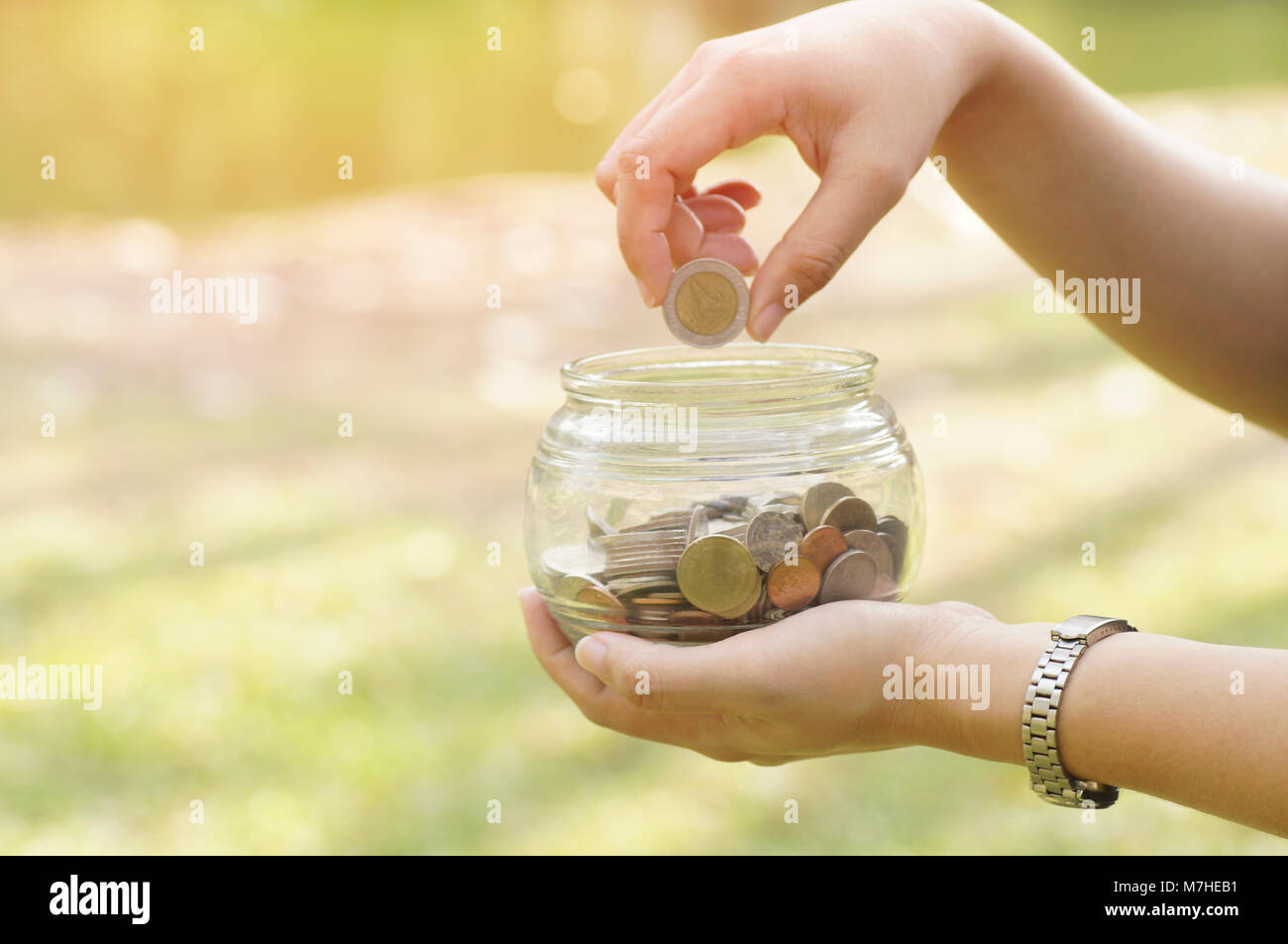 women's hand put money coins in glass bottle for save and donation ...
