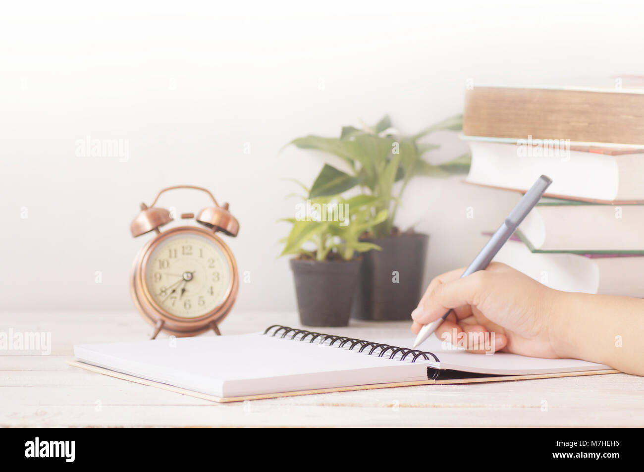 hand writing on note paper at working table with alarm clock, plant and ...