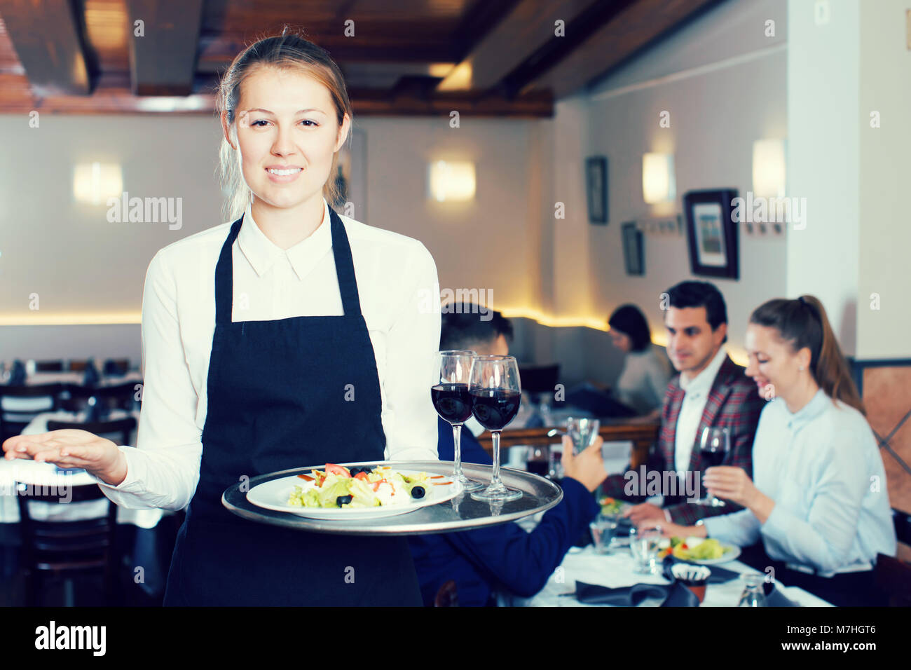 Portrait of smiling waitress with serving tray meeting restaurant ...
