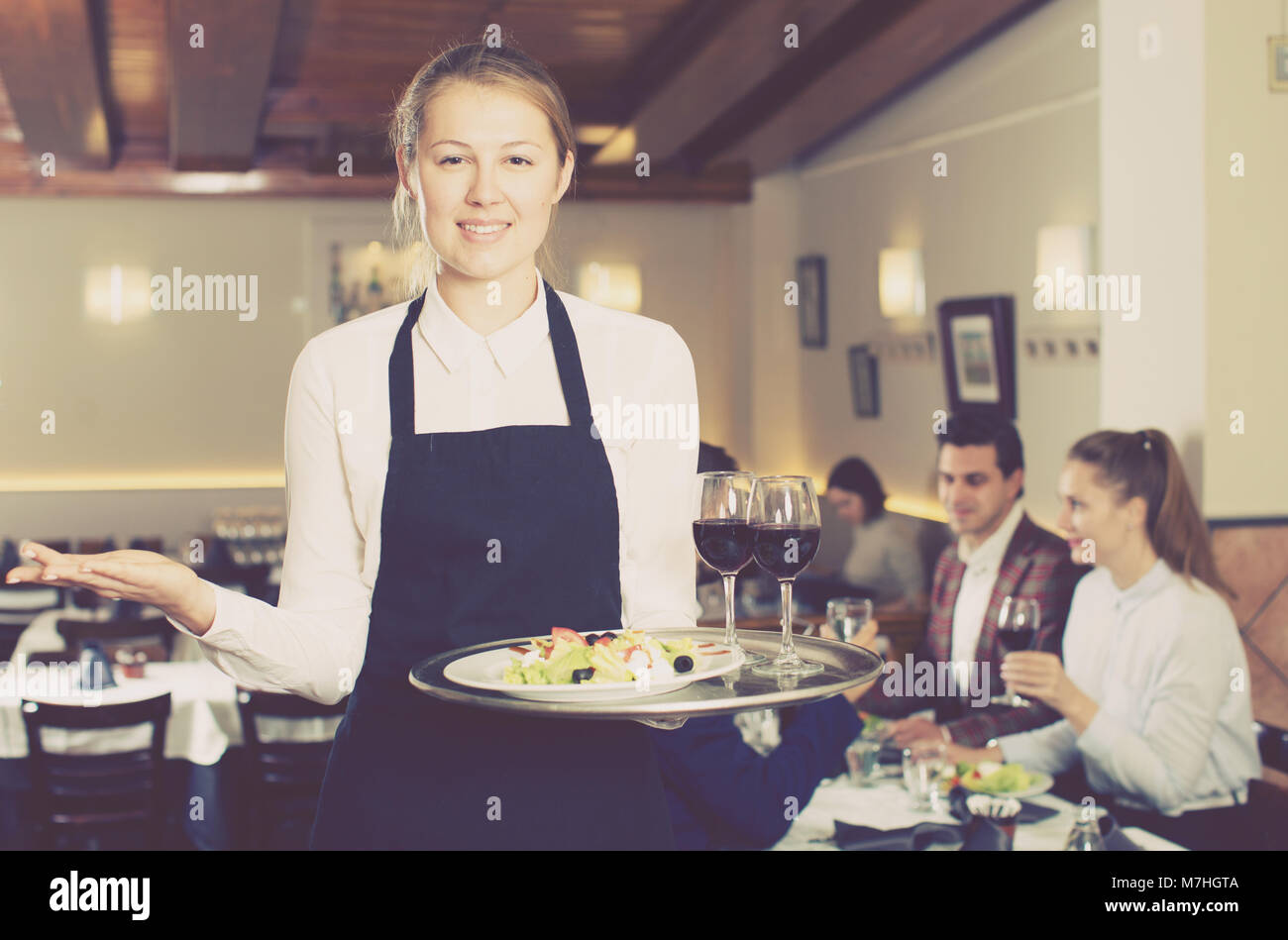 Attractive young waitress with serving tray welcoming to restaurant ...