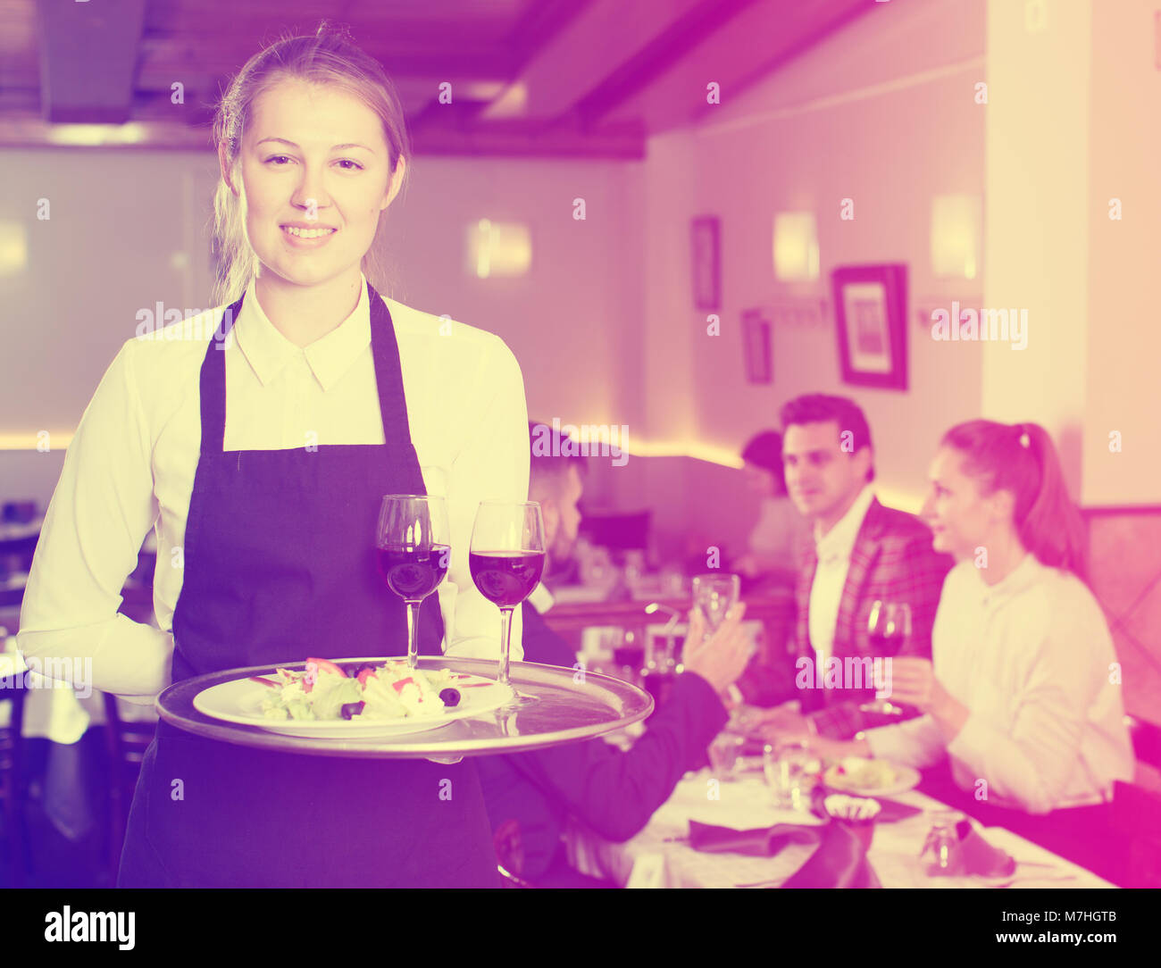 Attractive young waitress with serving tray welcoming to restaurant ...