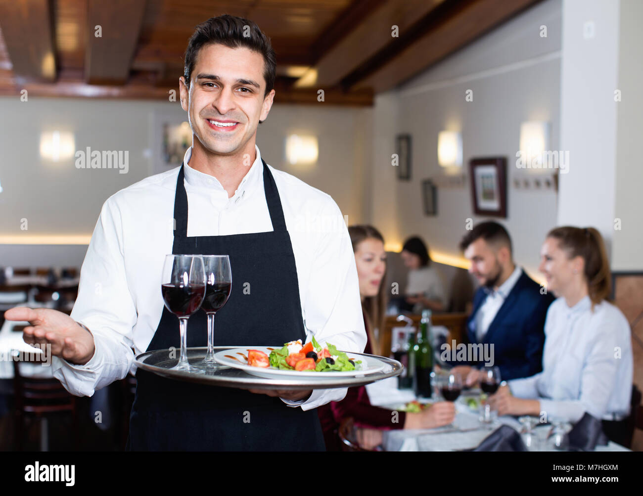 Portrait of glad smiling waiter with serving tray meeting restaurant ...
