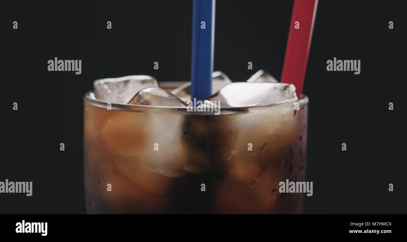 two straws in cola with ice cubes in glass over black background, wide ...