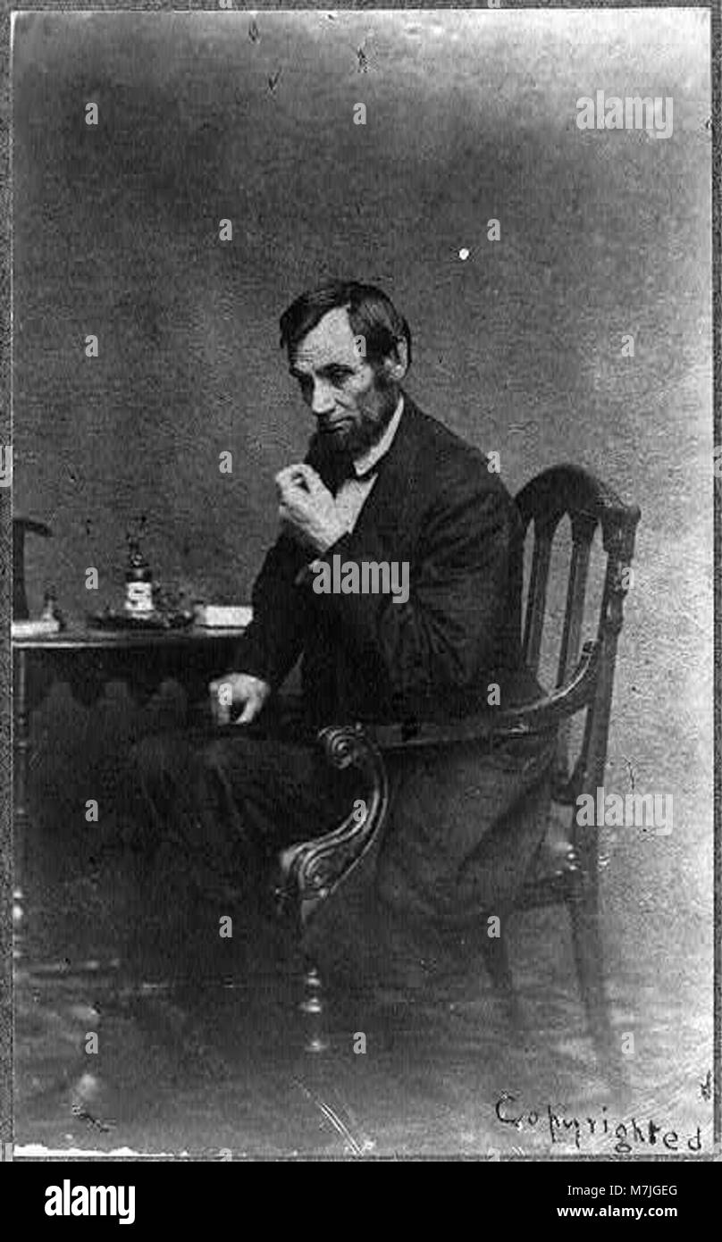 Photograph of Abraham Lincoln seated beside a small table, captured in ...