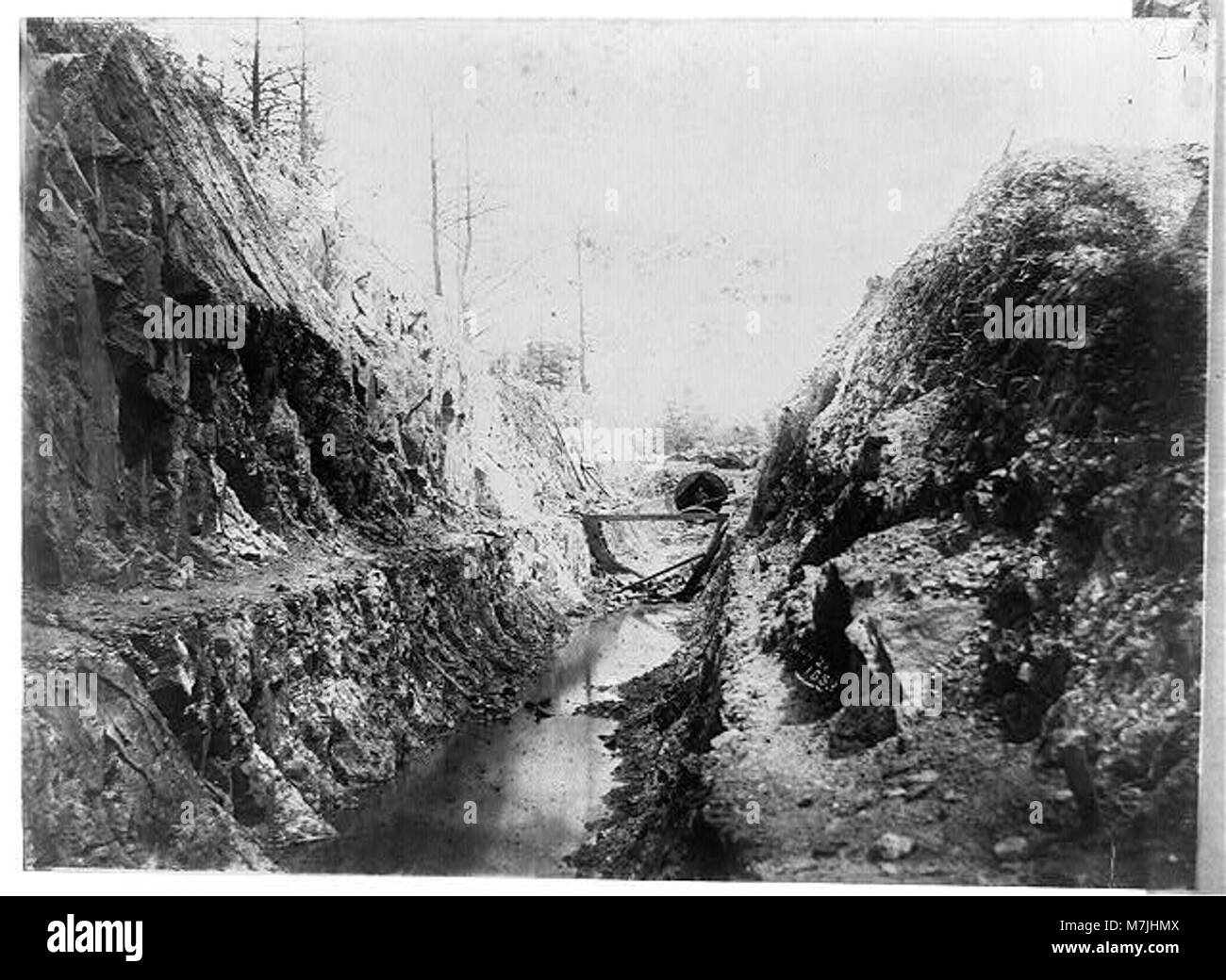 This photograph depicts a water-filled ditch leading to a tunnel, with ...