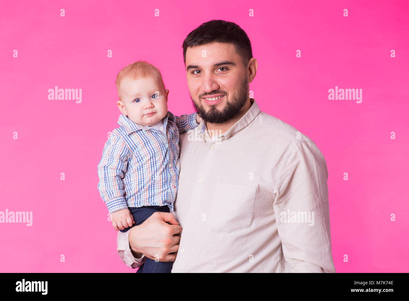 Happy father holding baby son in hands over pink background Stock Photo ...