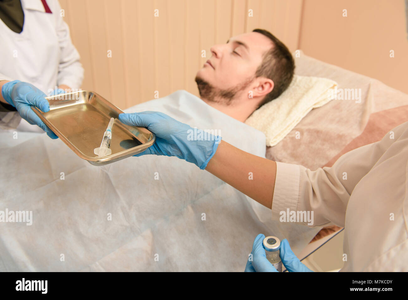 Doctor takes a syringe. Male patient during beauty procedure in surgery ...
