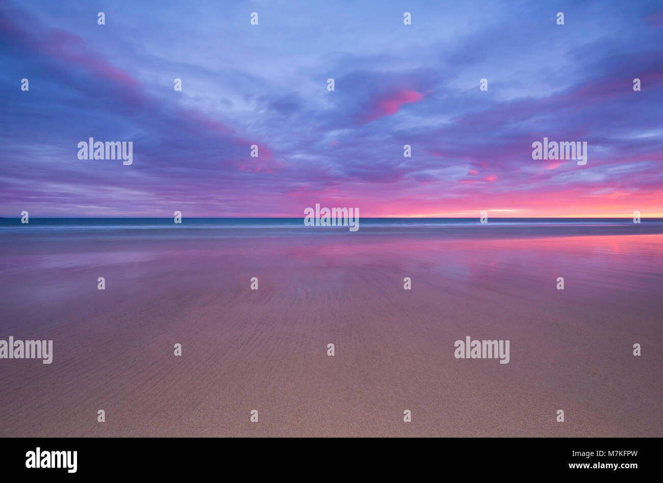 A beautiful pink and blue sunset reflected in the wet sand on a beach ...
