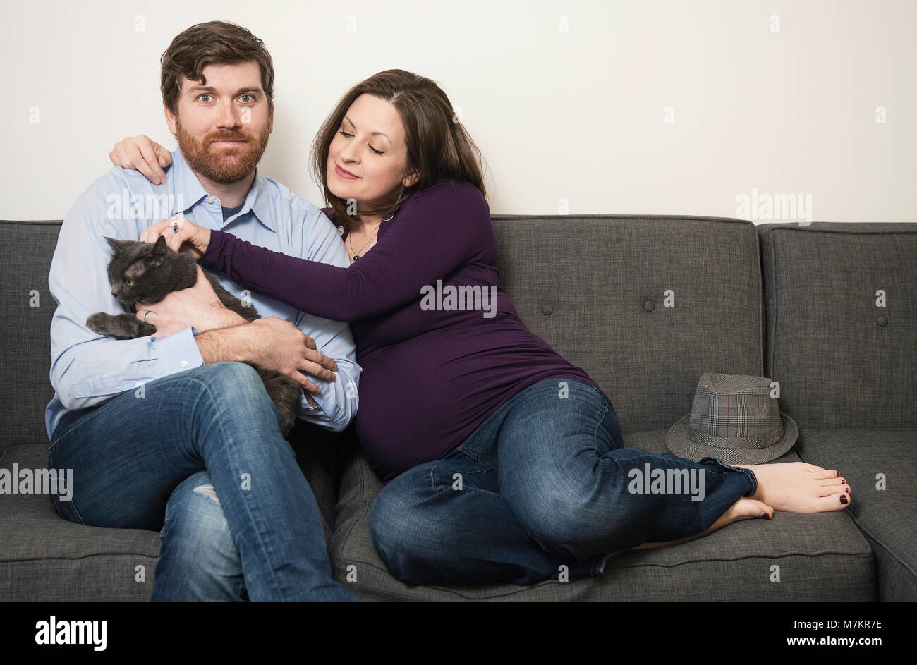 An expectant couple sitting on a sofa with their pet cat Stock Photo ...