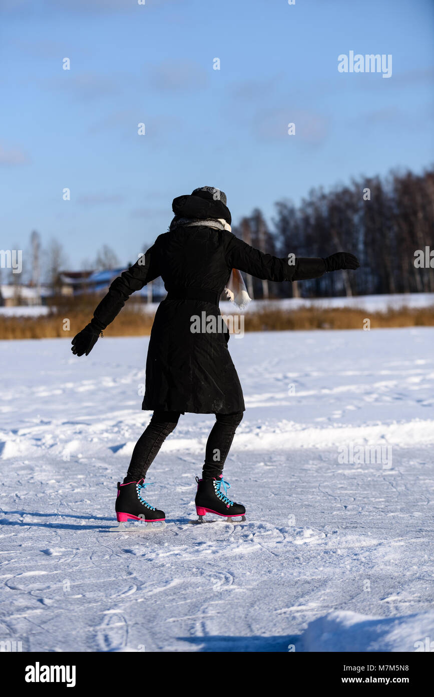 young woman in black coat skating on the frozen lake in snow with ...