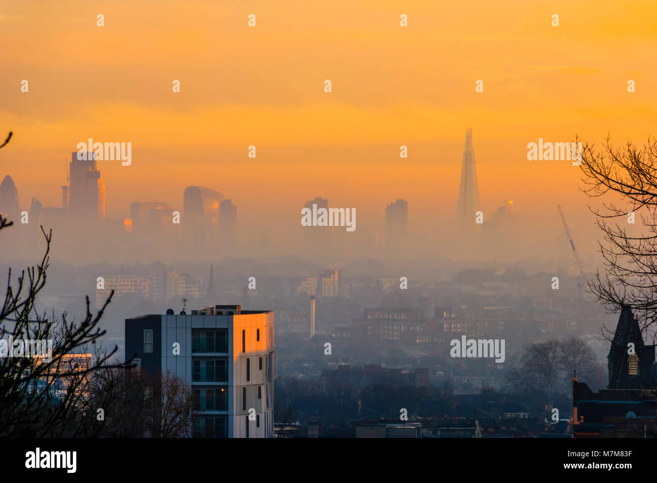 An orange sky over the City of London skyline, veiled by mist and ...