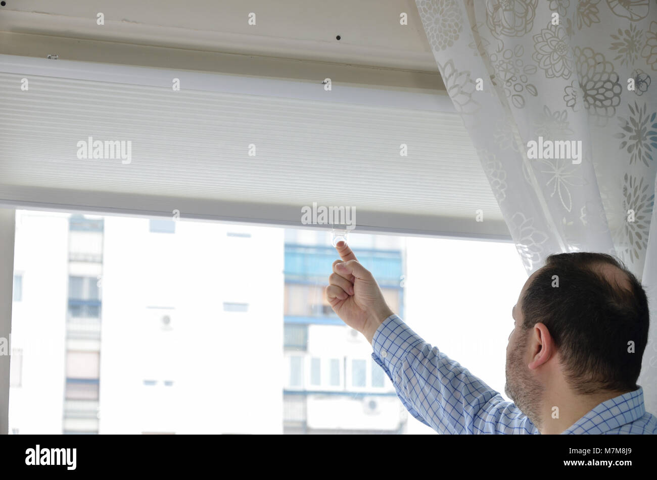 Man pulling down a white blind on a window Stock Photo - Alamy