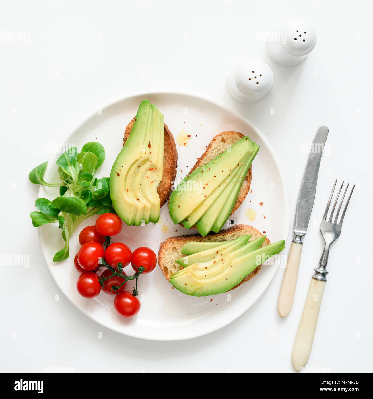 Avocado toasts, cherry tomatoes and salad on white plate, top view ...