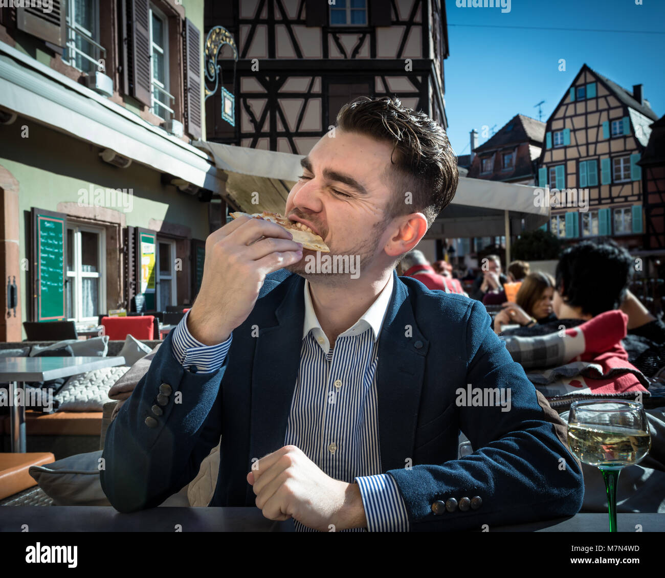Very hungry man eats pizza in cafe outdoors. Young guy in a suit is ...