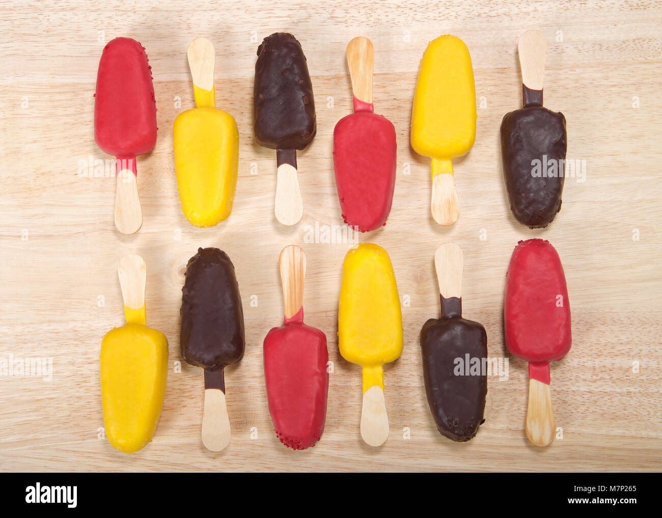 One dozen colorful candy covered cake popsicles on a light wood table ...