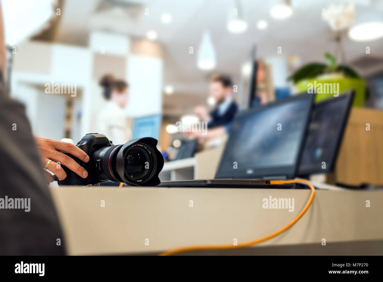 Hand of the camera operator touching a modern DSLR, laptop visible in ...