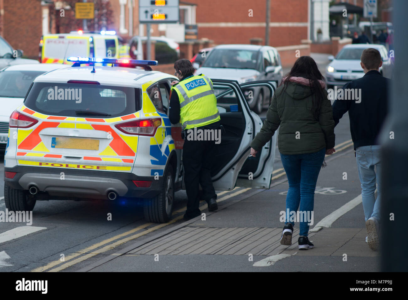 policeman enters vehicle with blue lights flashing and police riot van ...