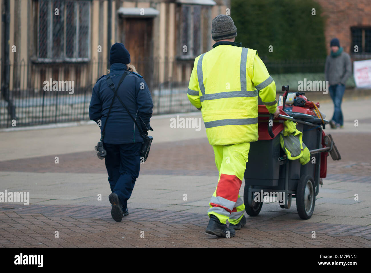 street sweeper walks down road pushing ref and grey barrow with ...