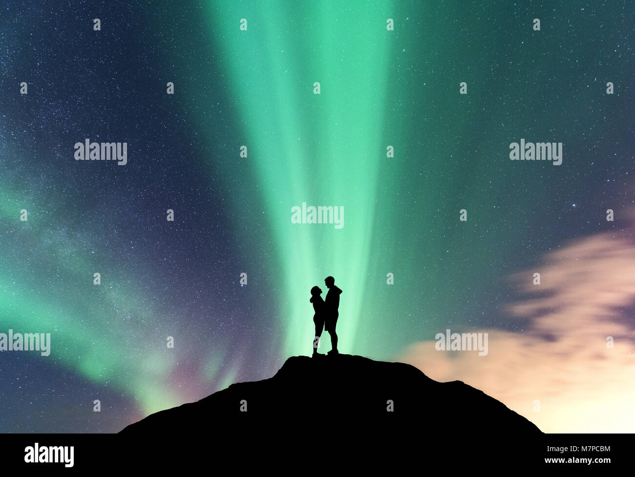 Aurora and hugging couple on the mountain peak. Landscape with night ...