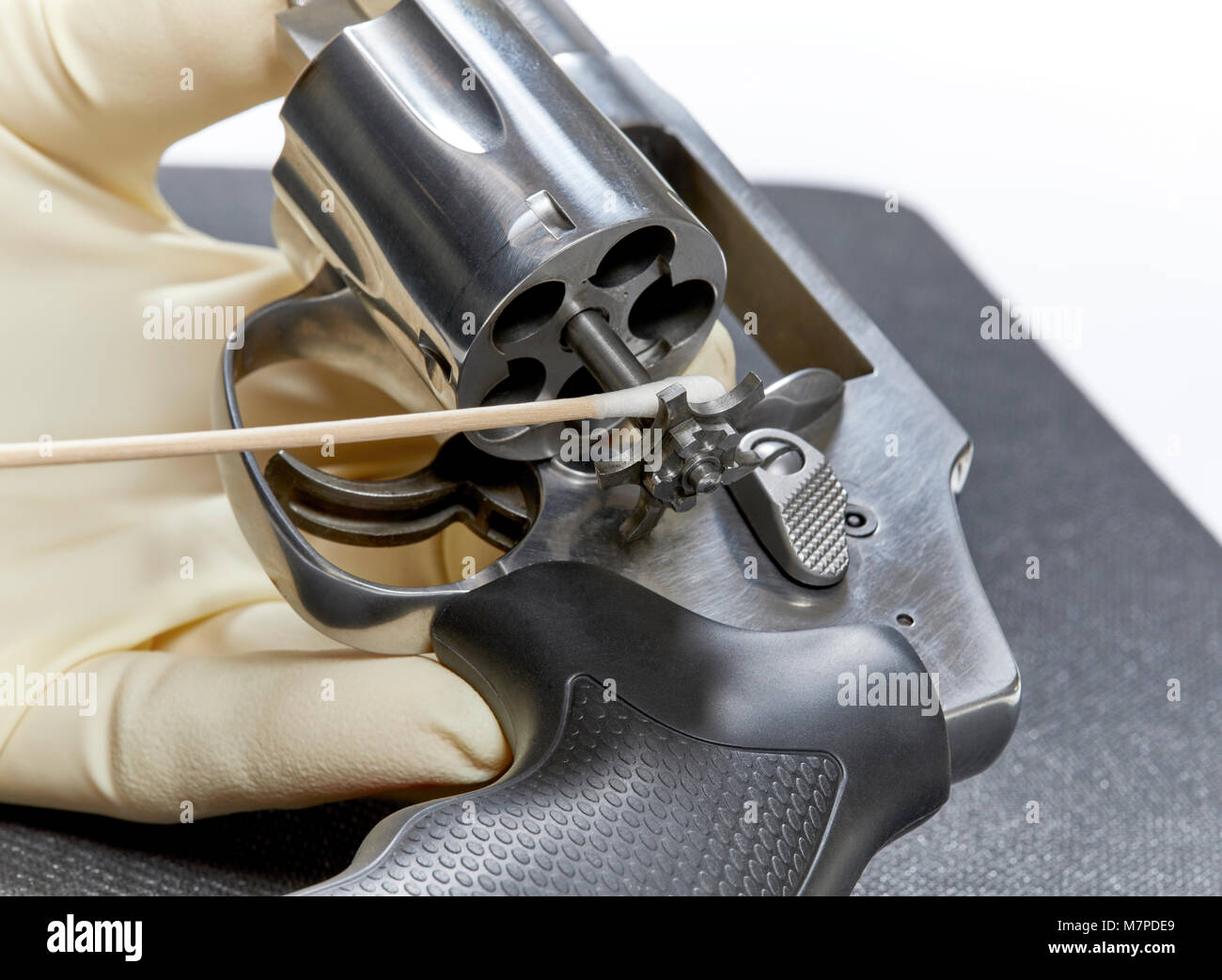 A gloved hand using a cotton swab to clean the ejector on a snubnose ...