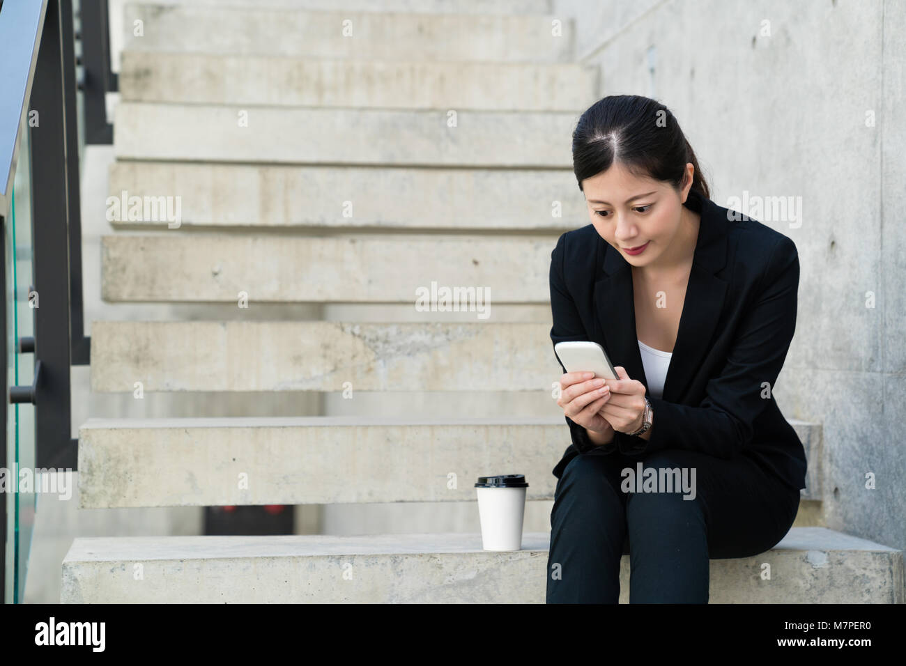 Smiling business woman sitting on the stairs communicating to friends ...