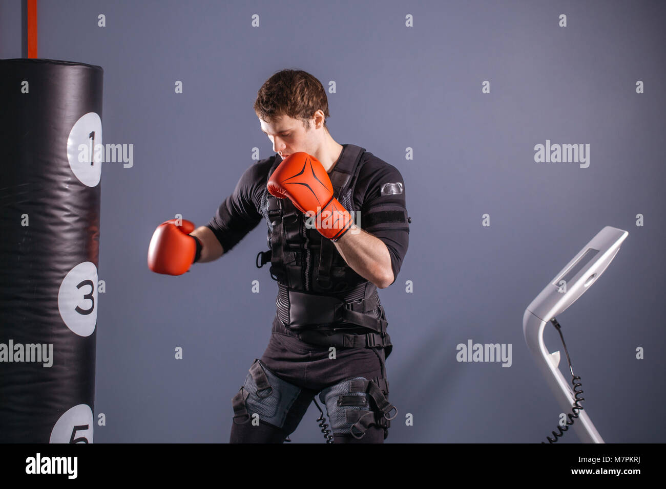 Man in boxing gloves. boxer wearing ems suit training with punching bag ...