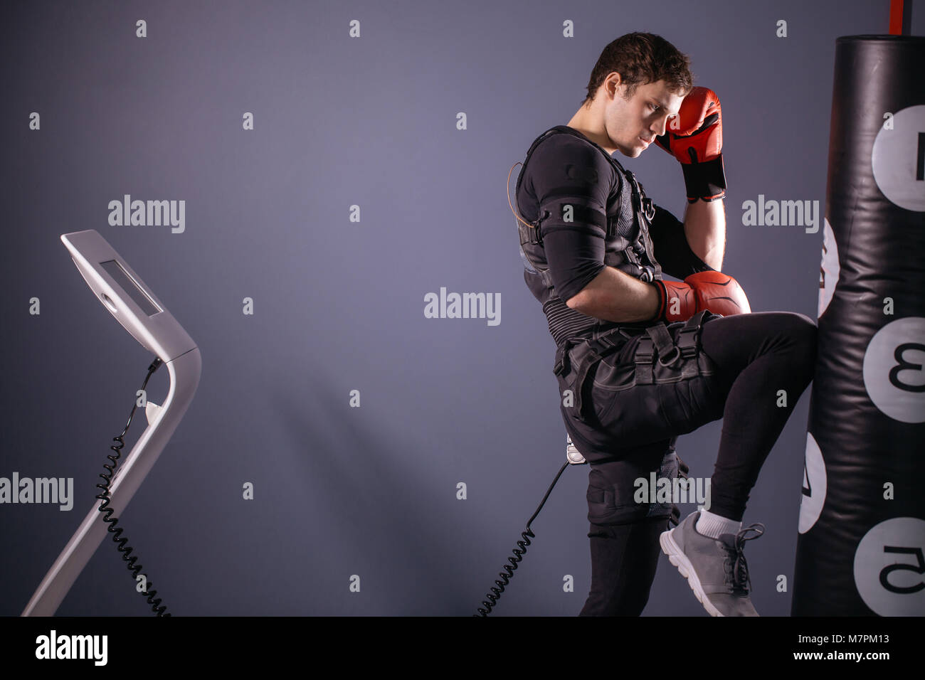 Fit man in boxing gloves training knee kick. kickboxer wearing ems suit ...