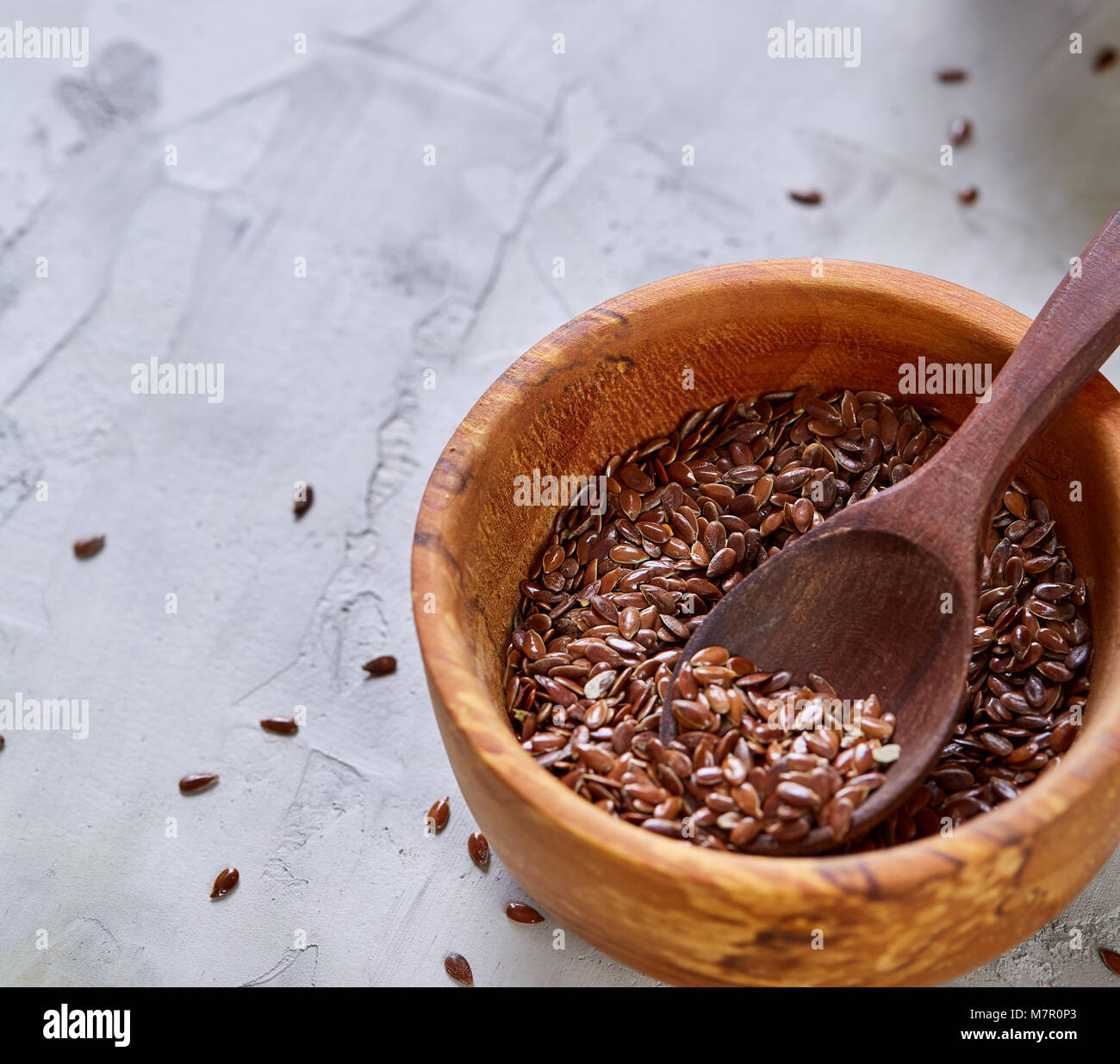 Flax seeds in clay ceramic bowl and flaxseed oil in transparent glass bottle on light textured ...