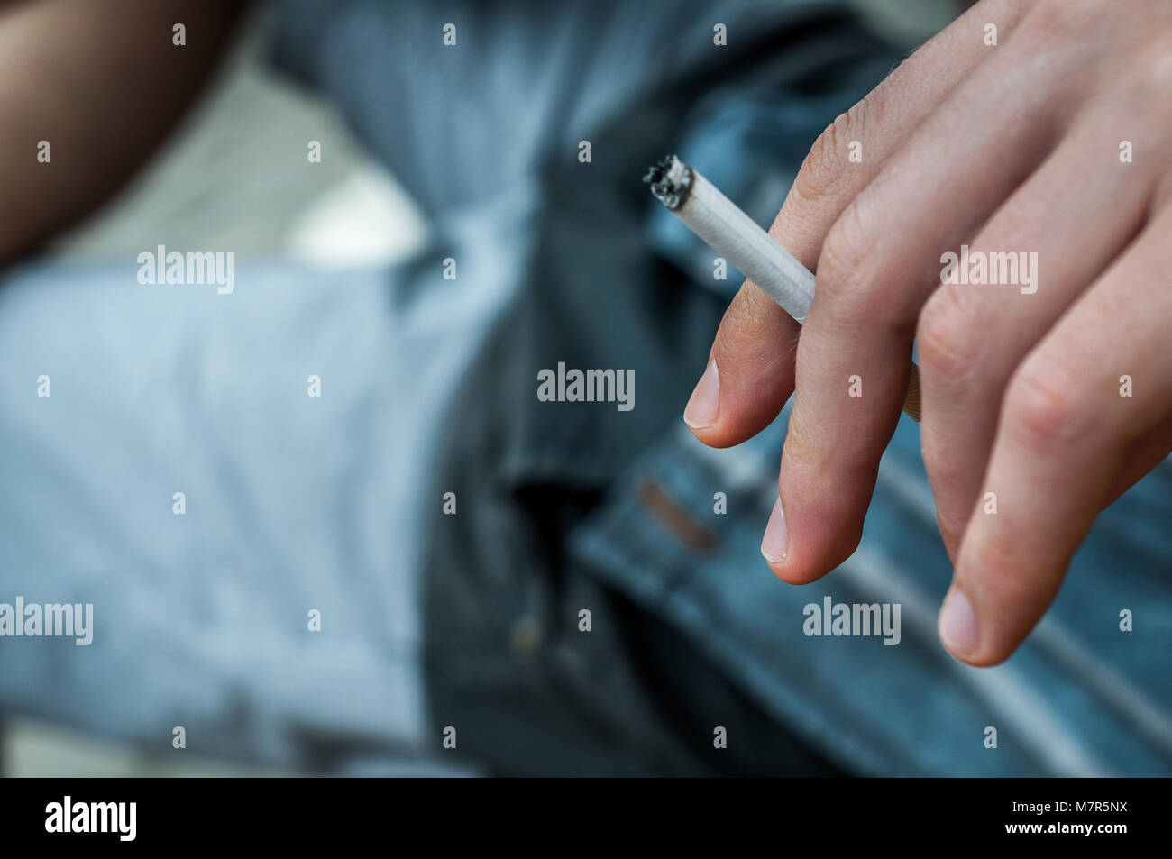 Teenage holding cigarette in his hand closeup outdoor. Cropped shot ...