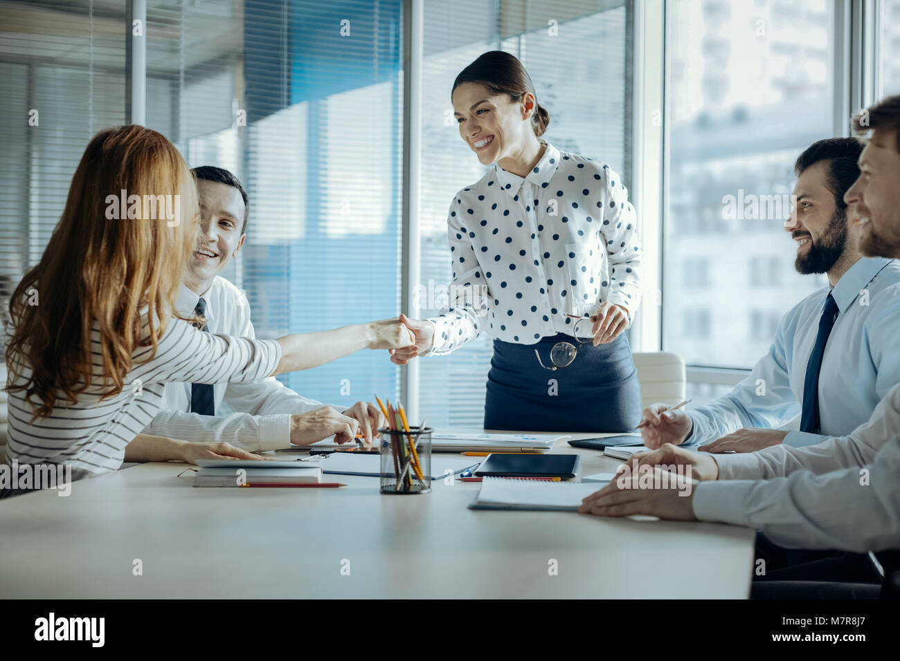 Cheerful boss shaking hands with her female colleague during meeting ...