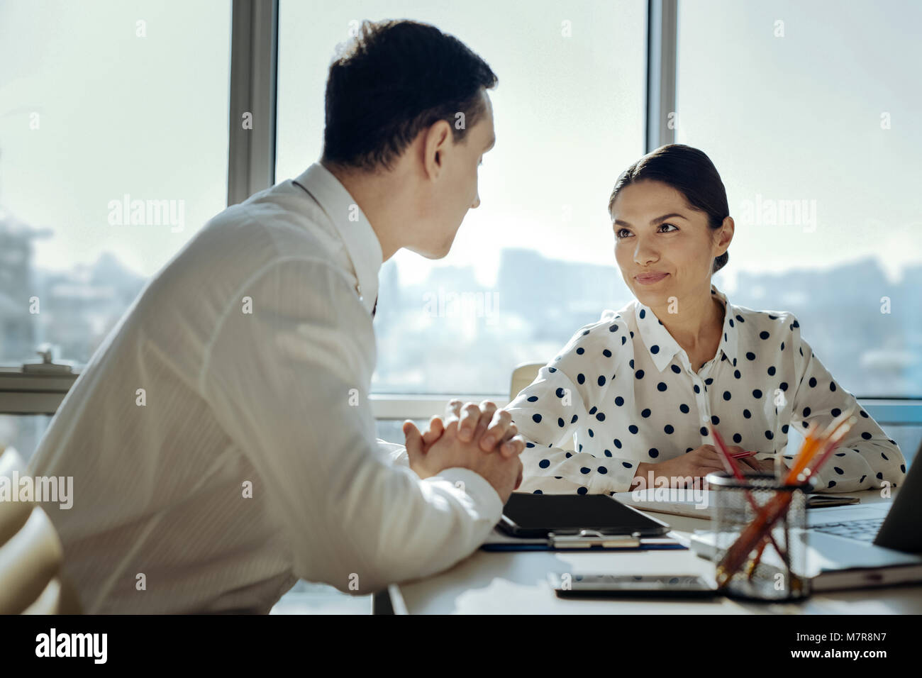Upbeat colleagues exchanging smiles while working on common project ...